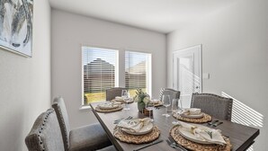 Uma sala de jantar com uma mesa comprida posta para seis pessoas, com jogos americanos trançados, pratos brancos e talheres.