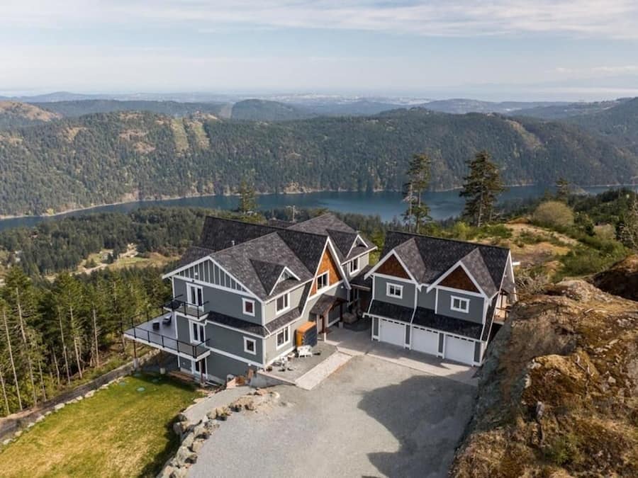 Uma casa moderna de dois andares com uma grande entrada e vista para um lago e colinas arborizadas.