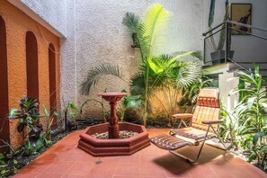 Um pátio com uma fonte, uma cadeira e diversas plantas.