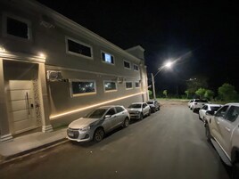 Um edifício de vários andares com uma fileira de carros estacionados na rua.