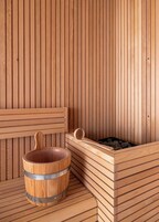 Uma sauna de madeira com uma banheira de madeira, um banco de madeira e um recipiente de madeira com uma faixa de metal.