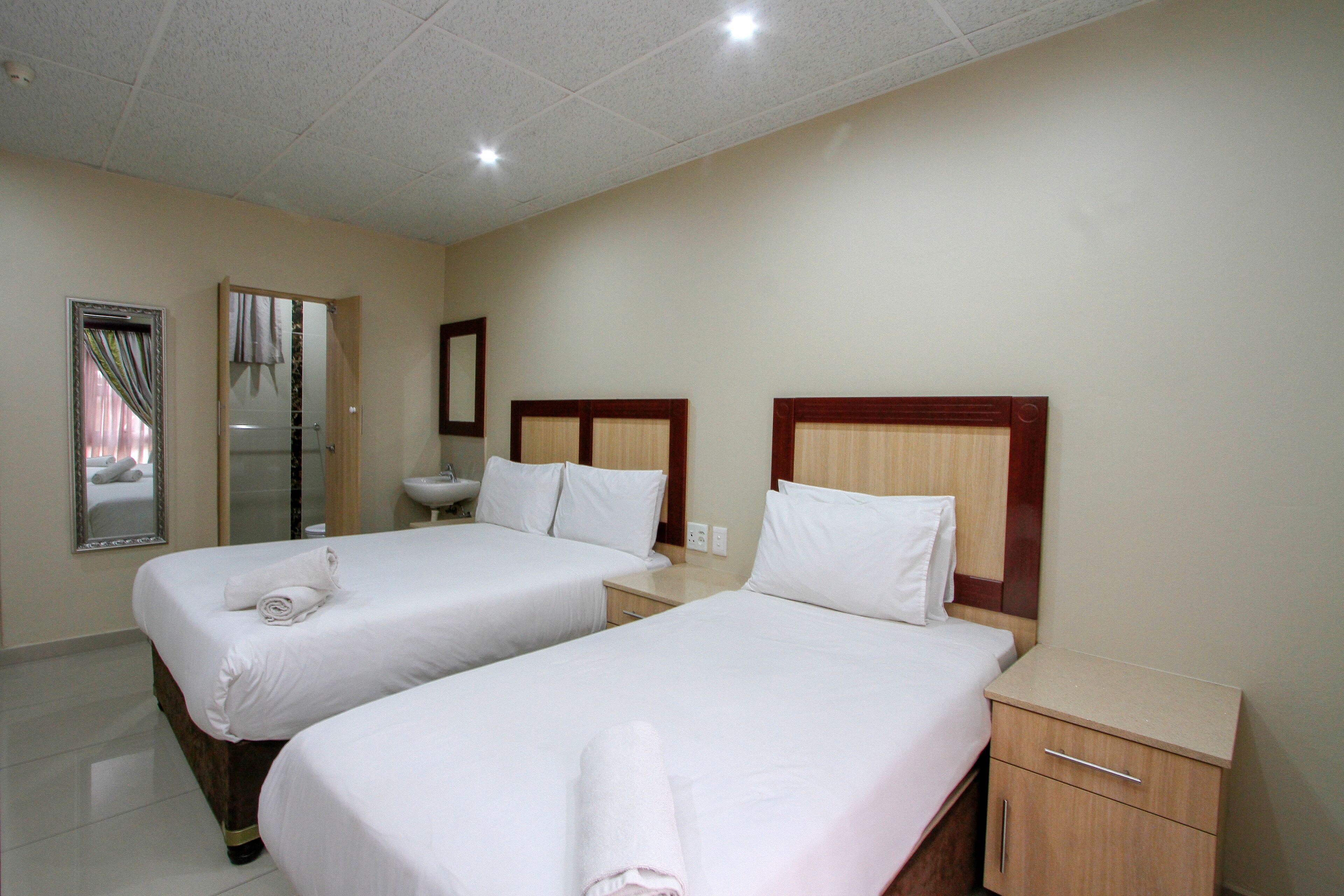 Quarto de hotel com duas camas, um banheiro e um espelho.