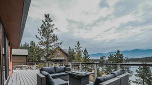 Um terraço com mobiliário de vime e vista para um lago e montanhas.
