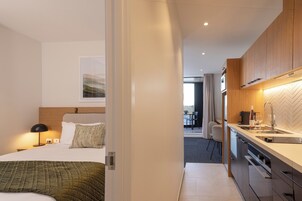 Quarto de hotel moderno com cama, luminária de cabeceira e vista para a sala de jantar.