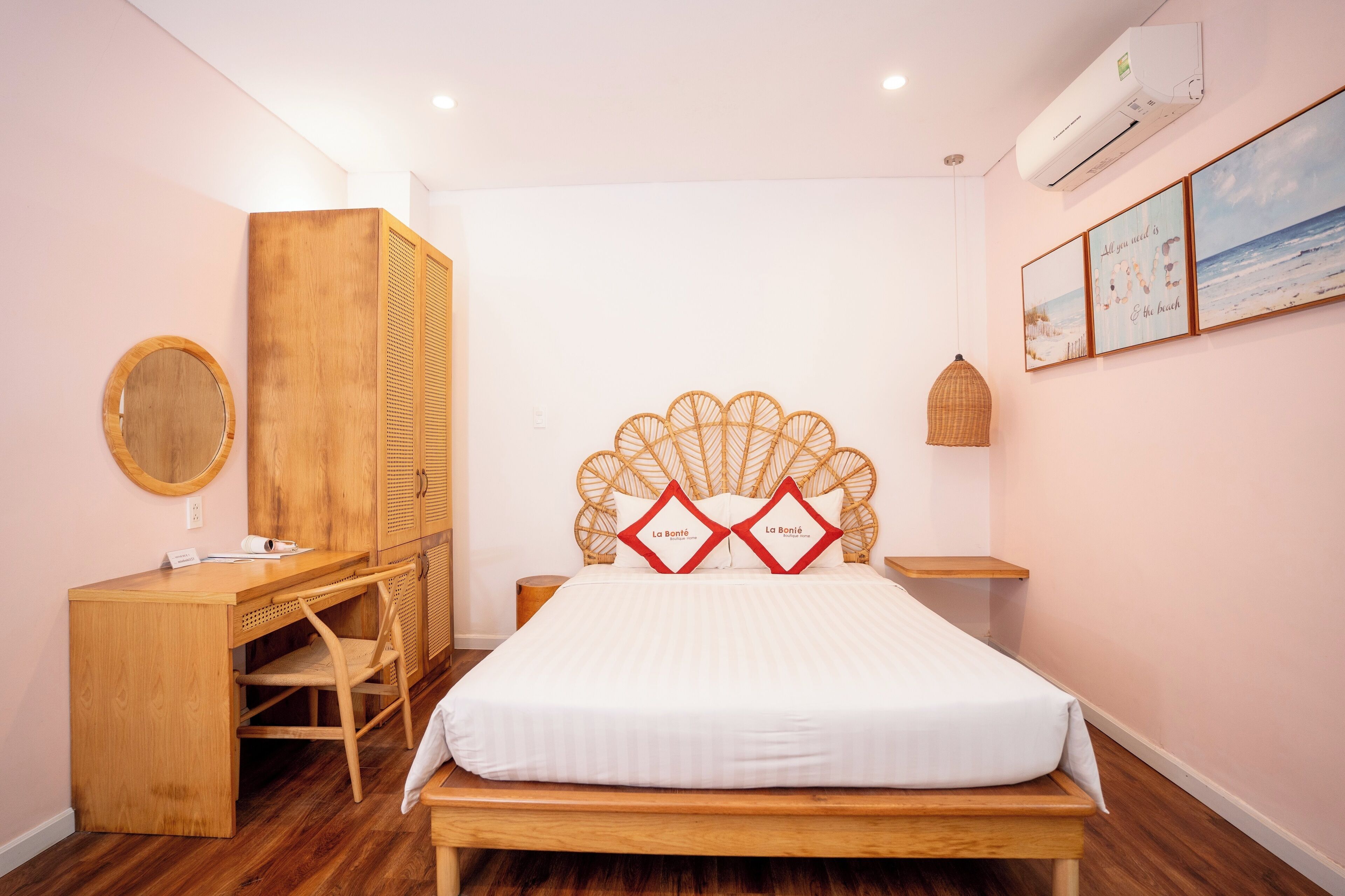 Quarto com cama de madeira, escrivaninha de madeira, espelho redondo, cabeceira de vime e ar-condicionado fixado na parede.