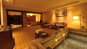 Um saguão de hotel com balcão de recepção, área de estar e uma pequena piscina interior.
