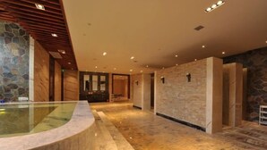 Um hall de hotel com piso de mármore, paredes de pedra e uma área de recepção com balcão de vidro.
