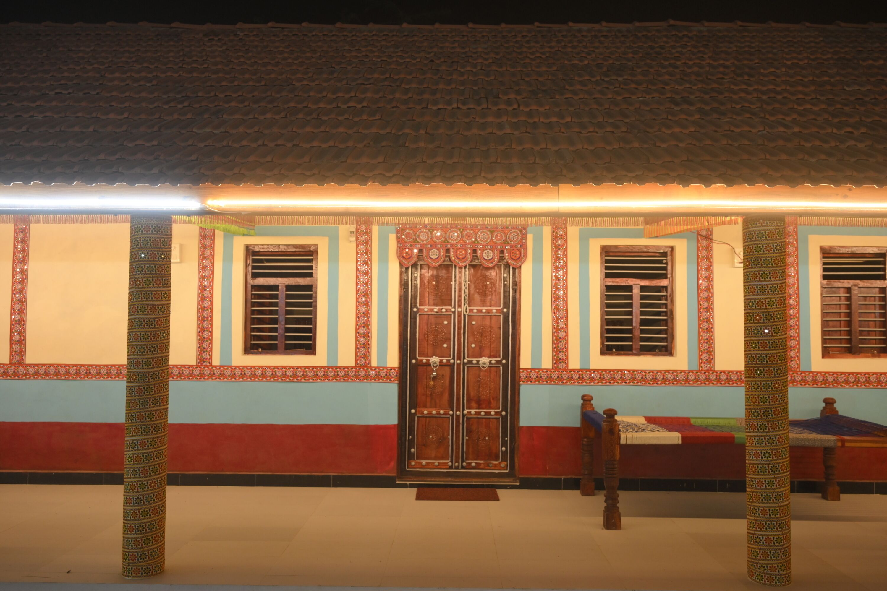 Um edifício tradicional com telhado em telhas, porta de madeira central com painéis decorativos e duas janelas com persianas.