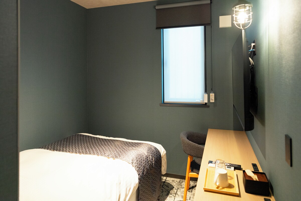 Quarto de hotel com cama, escrivaninha, cadeira e janela.