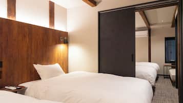 Quarto de hotel com duas camas, cabeceiras de madeira, uma porta escura e uma pequena mesa com um controle remoto.