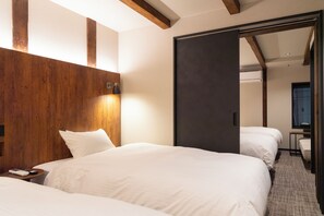 Quarto de hotel com duas camas, cabeceiras de madeira, uma porta escura e uma pequena mesa com um controle remoto.