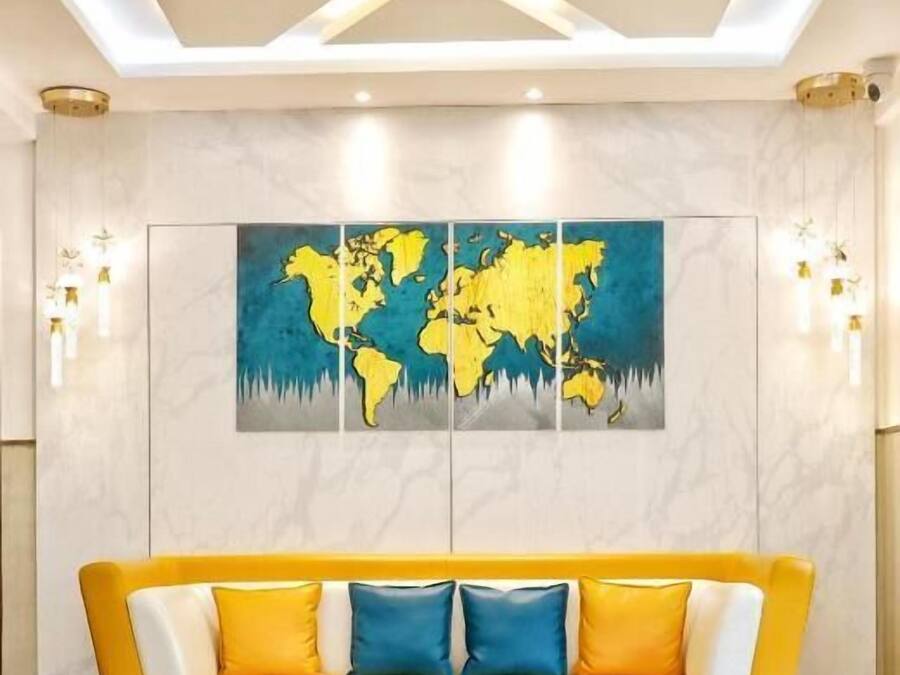 Um lobby moderno com um sofá amarelo, uma obra de arte com um mapa-múndi e um design geométrico no teto.