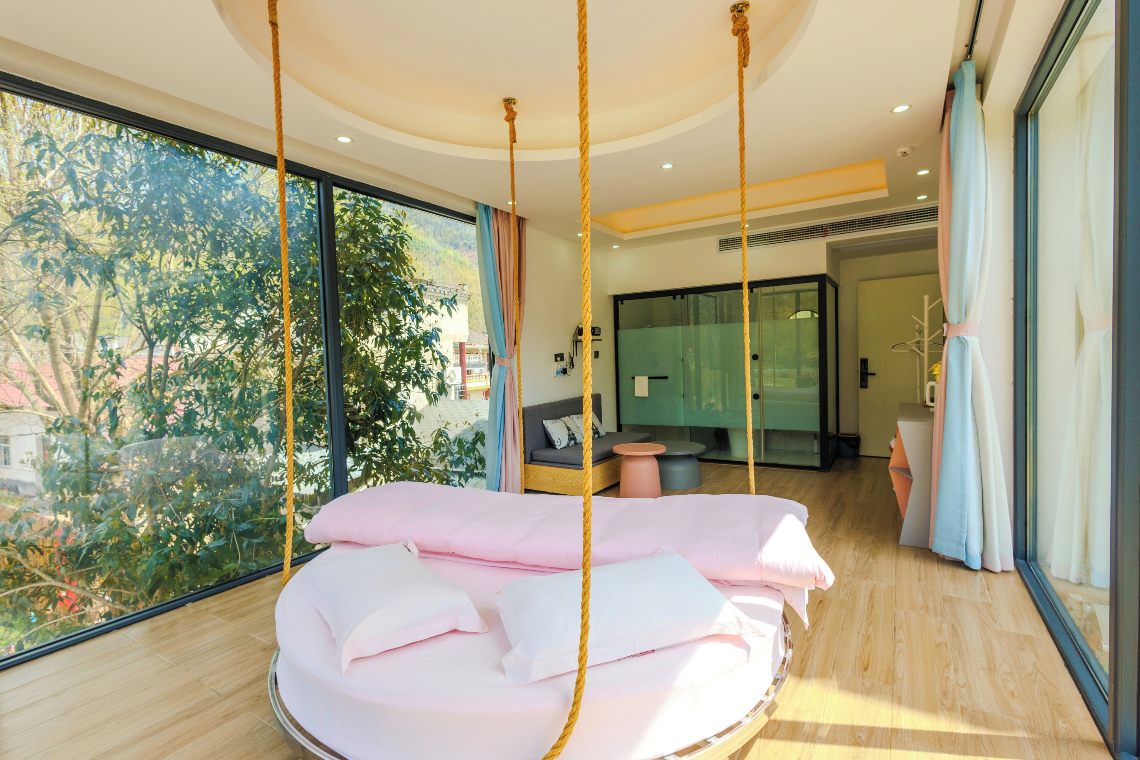 Quarto moderno com cama redonda, grandes janelas e vista para o verde lá fora.
