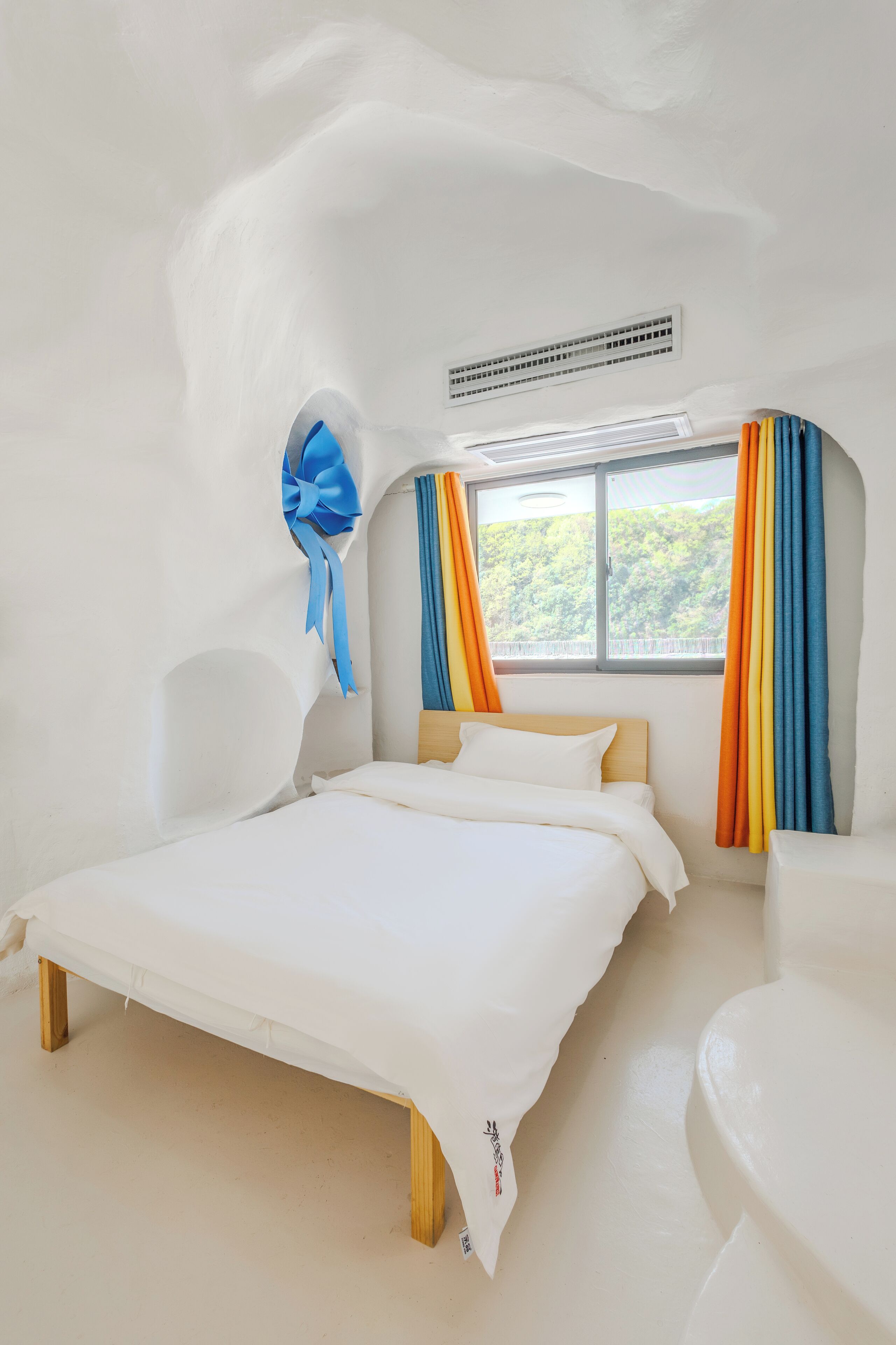 Quarto com cama, cadeira, janela com cortinas e ar condicionado.