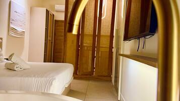 Quarto de hotel com uma banheira grande e branca, armário de madeira e uma televisão na parede.