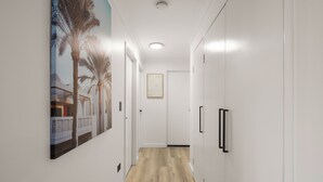 Um corredor estreito com soalho de madeira, paredes brancas e um quadro emoldurado à esquerda.