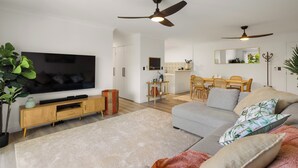 Uma sala de estar moderna com televisão de tela plana, um sofá cinza, um armário de madeira e um ventilador de teto.