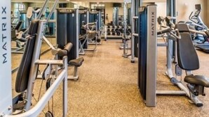 Uma academia com diversos equipamentos de exercício, incluindo máquinas de peso e esteiras, dispostos em fileiras.