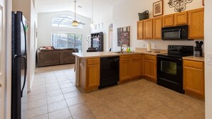 Uma cozinha moderna com armários de madeira, uma lava-louças preta, um fogão preto e um micro-ondas. Há uma janela grande que oferece luz natural e vista para o exterior.