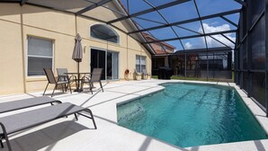 Piscina com área de estar coberta, incluindo espreguiçadeiras e uma mesa.