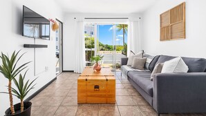 Uma sala de estar moderna com um sofá cinzento, uma mesa de centro de madeira e uma televisão de ecrã plano fixada na parede.