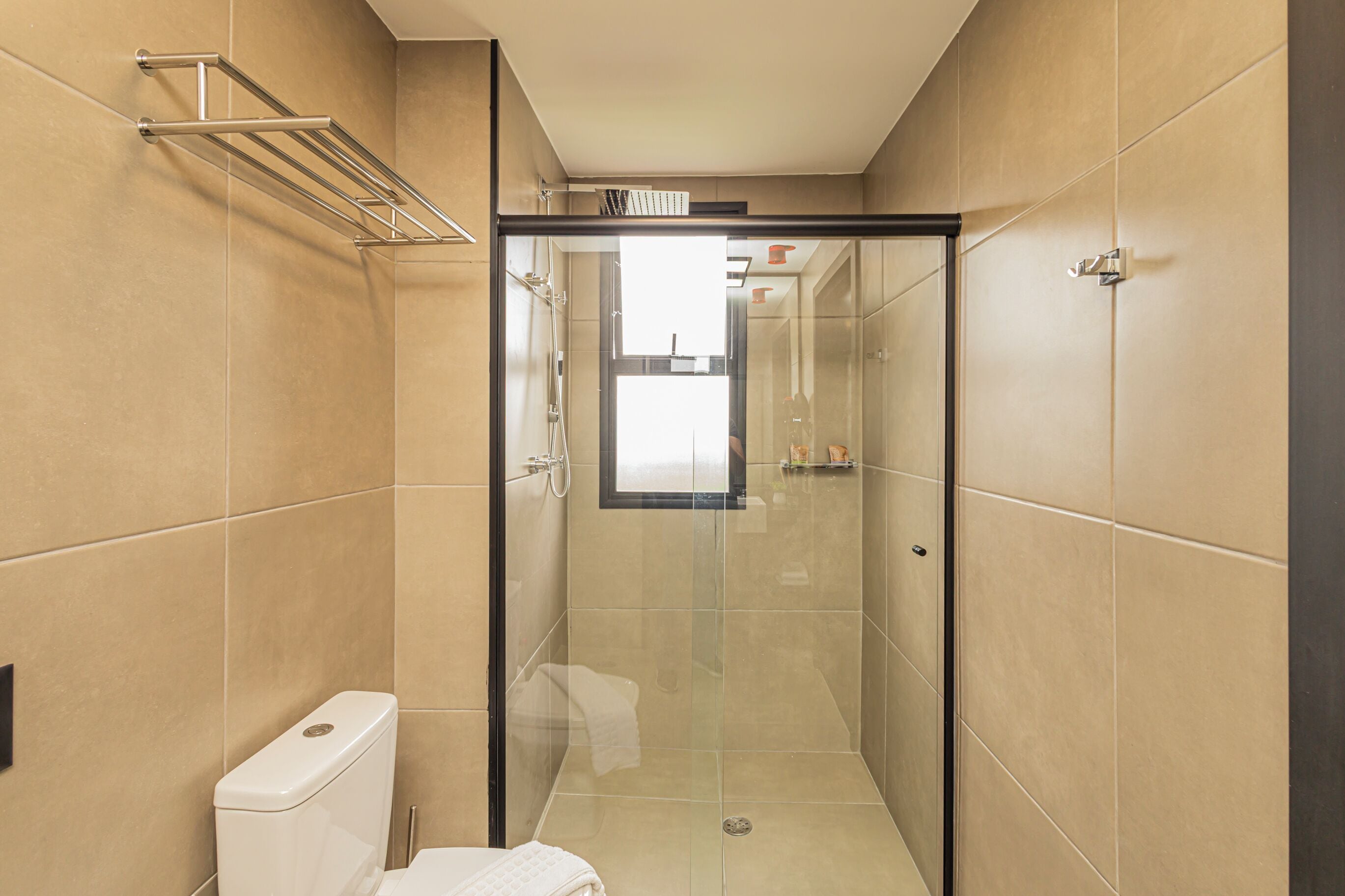 Uma casa de banho moderna com chuveiro de vidro, sanita e suporte para toalhas.