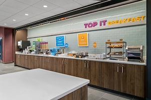 Espaço de café da manhã com um aviso indicando 'TOP IT BREAKFAST' e diversas opções de comida, como panquecas e ovos.