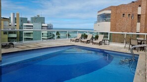 Uma piscina no terraço com espreguiçadeiras e vista para o oceano.