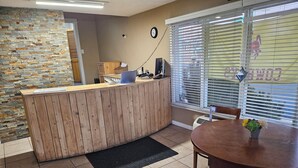Uma área de recepção com uma mesa de madeira, um relógio, uma janela com persianas e piso ladrilhado.