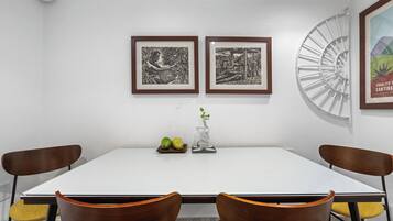 Uma área de refeições com uma mesa branca, duas obras de arte em preto e branco emolduradas, uma planta em vaso e uma escada em espiral.