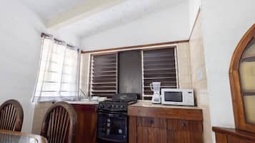 Uma cozinha compacta com fogão, micro-ondas e liquidificador, armários de madeira e uma janela com persianas.