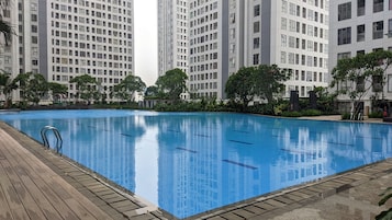 Piscina com deck de madeira, cercada por edifícios residenciais altos e vegetação.