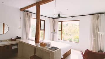 Quarto com uma cama grande, uma escrivaninha de madeira, uma cadeira, um espelho e vista para o exterior.
