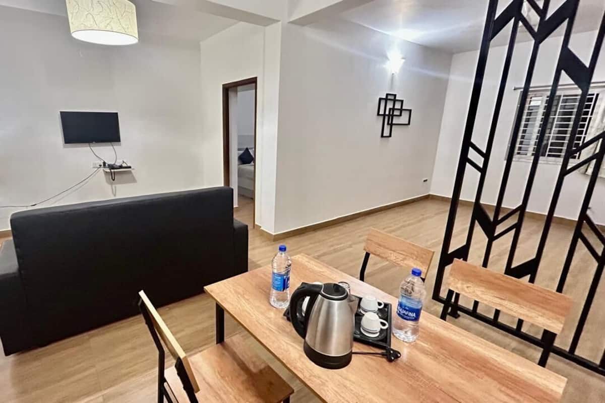 Quarto moderno com sofá preto, mesa de madeira e cadeiras, TV fixada na parede e escada com guarda-corrimão preto.
