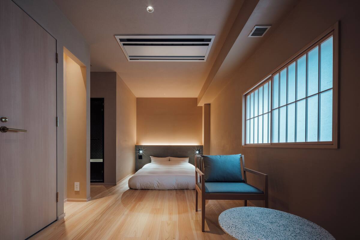 Um quarto com uma cama, uma cadeira, uma janela e uma porta.