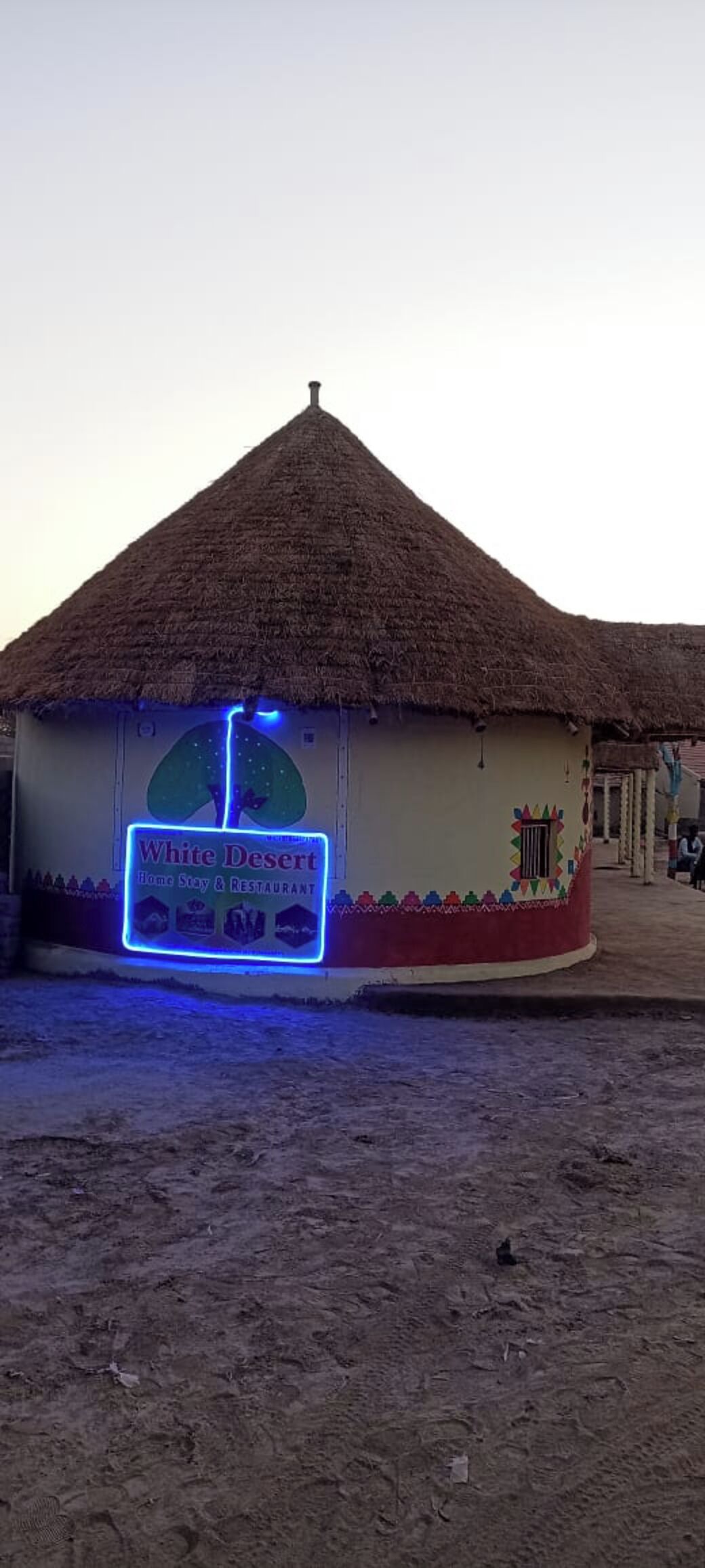 Um edifício com telhado de palha e uma placa com a inscrição "White Desert Home Stay & Restaurant".