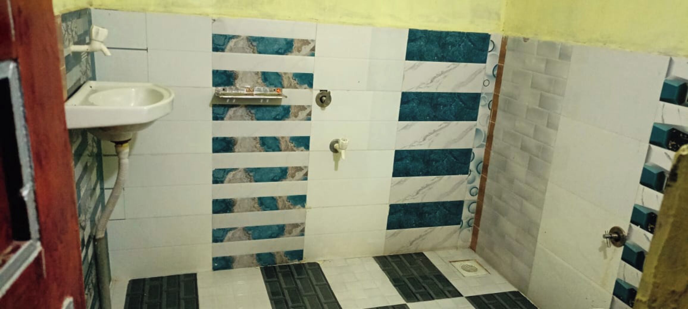 Um banheiro com pia, porta com puxador e paredes revestidas com azulejos azuis e brancos.