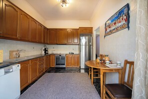 Uma cozinha com armários de madeira, uma geladeira de aço inoxidável, uma lava-louças e uma mesa de jantar com cadeiras.