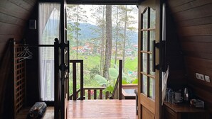 Um quarto de madeira com uma janela ampla, um banco de madeira e vista para uma paisagem verde com árvores e casas.