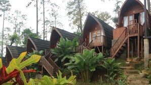 Fileira de cabanas de madeira com escadas externas, rodeadas por vegetação exuberante.