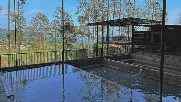 Piscina ao ar livre com deck de madeira e grade de metal, cercada por árvores e céu claro.