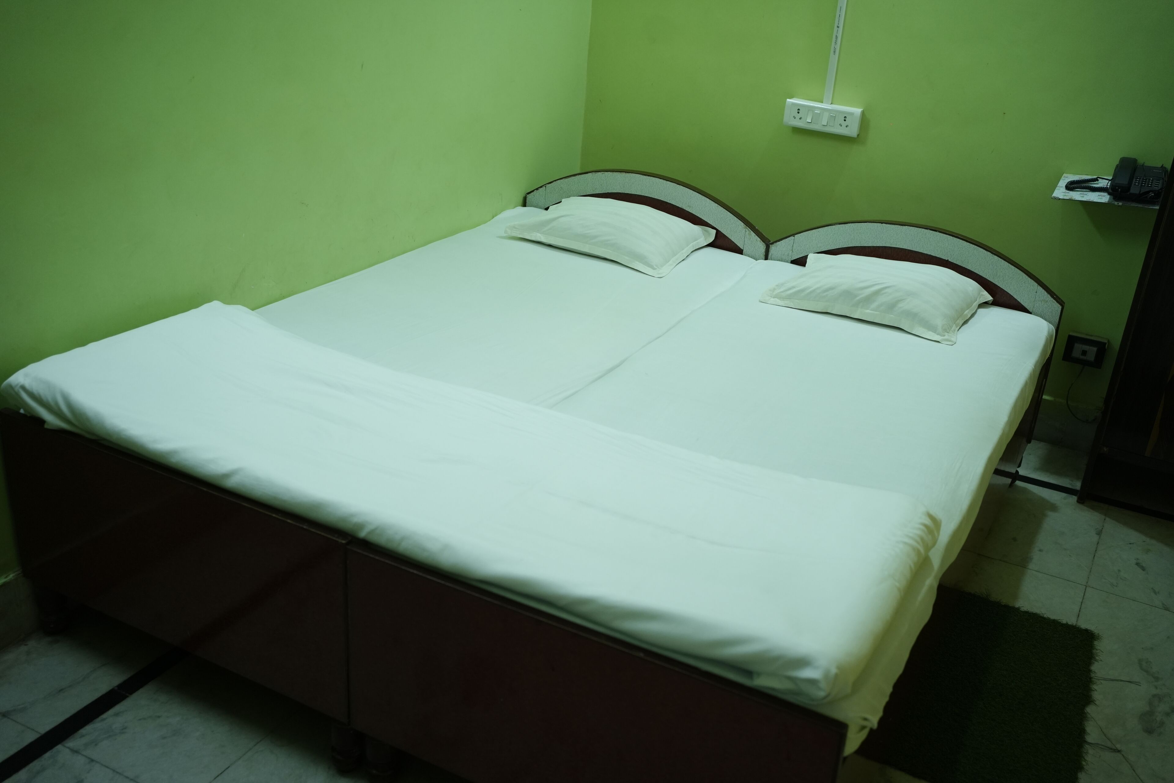 Quarto individual com uma cama de solteiro, cabeceira de madeira, colchão branco e parede verde.