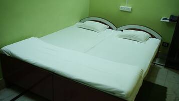 Quarto individual com uma cama de solteiro, cabeceira de madeira, colchão branco e parede verde.