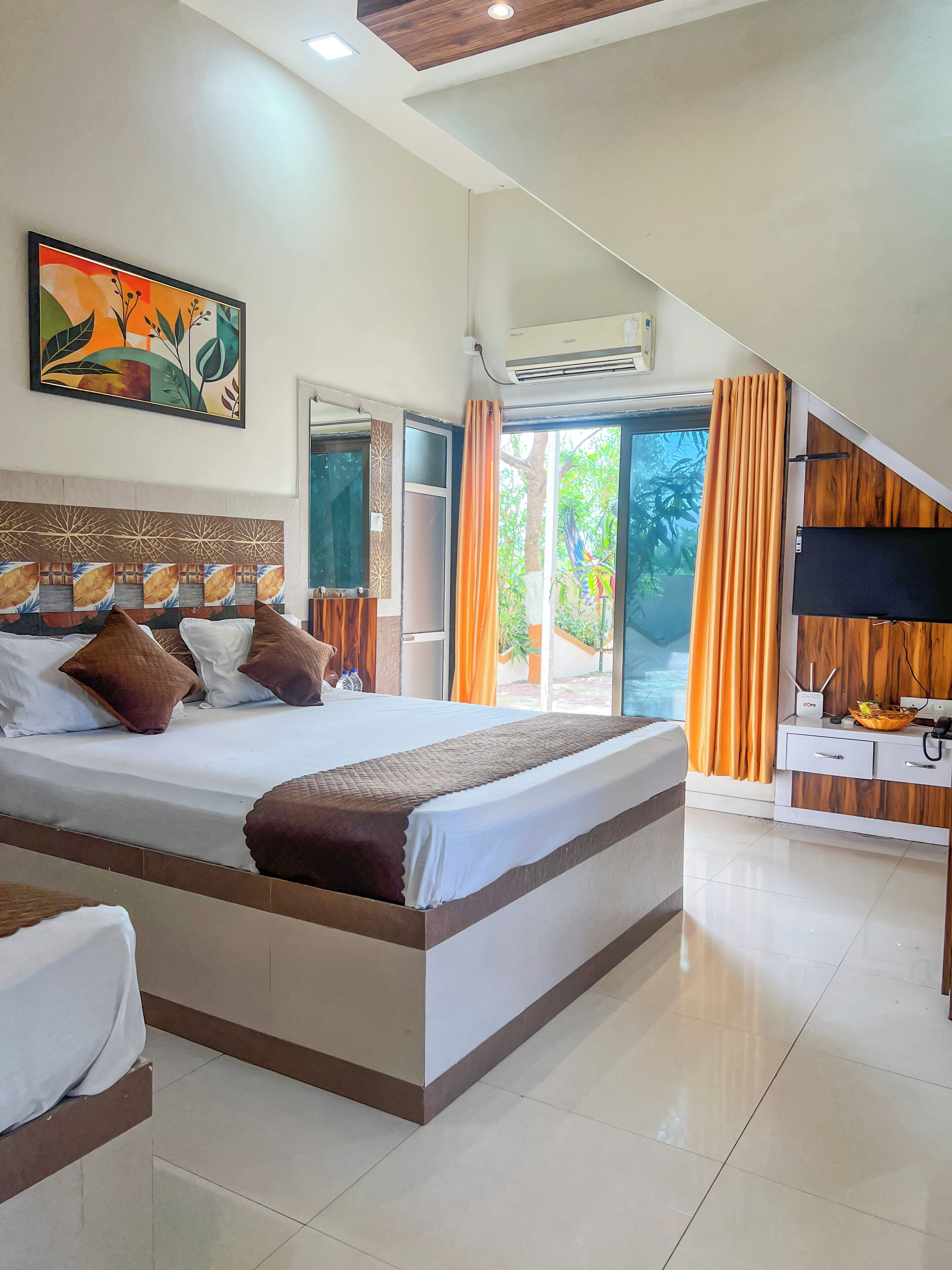 Quarto de hotel moderno com uma cama grande, televisão, escrivaninha com computador e vista para o exterior.