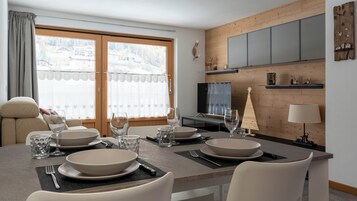 Uma sala de jantar com uma mesa posta para quatro pessoas, uma televisão e uma pequena árvore de Natal.