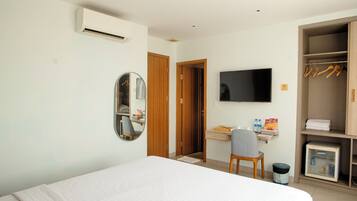 Quarto de hotel com cama, escrivaninha, cadeira, televisão, guarda-roupa e um pequeno frigorífico.