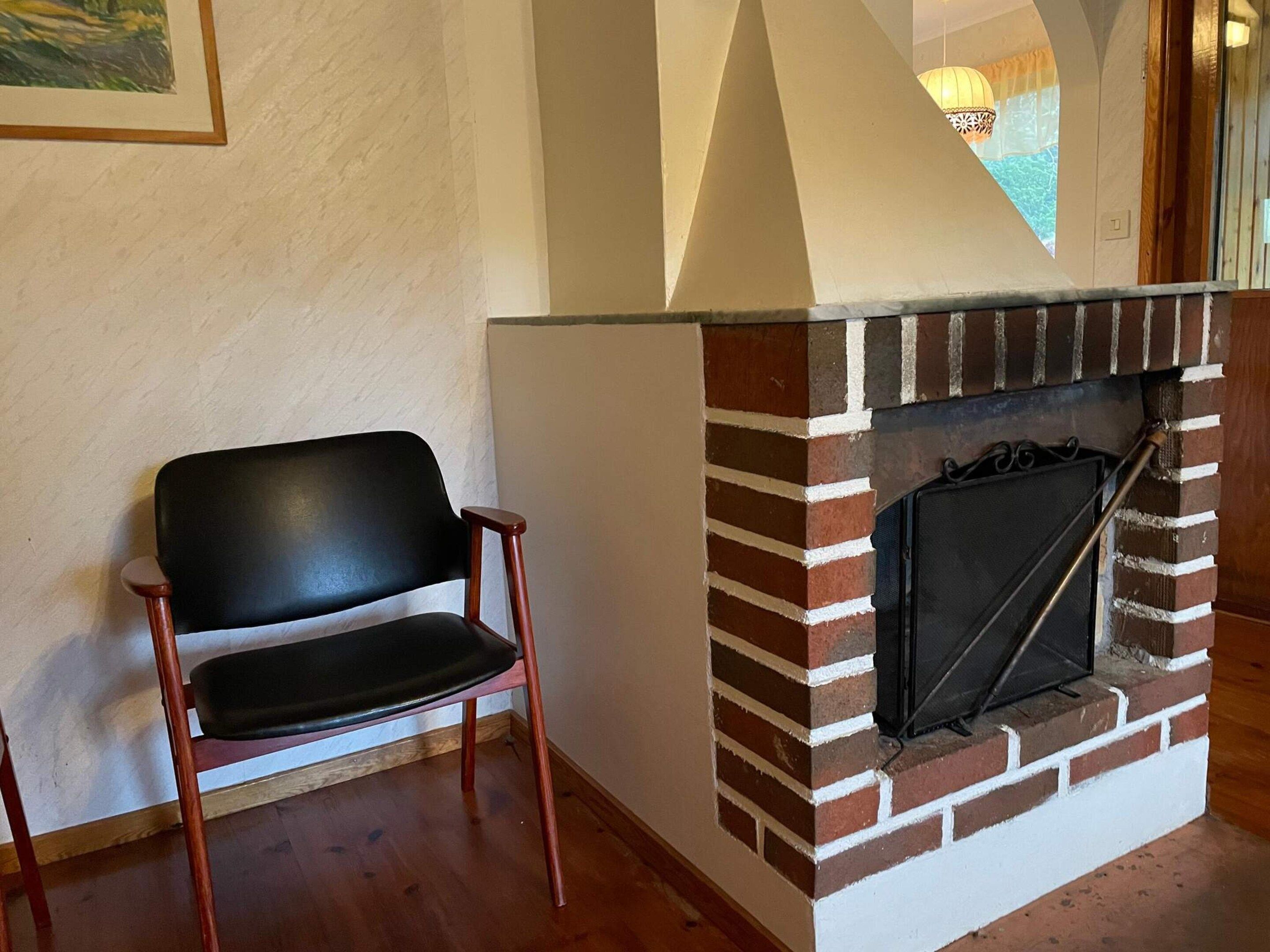Quarto com lareira de tijolos, uma cadeira de madeira e um quadro na parede.