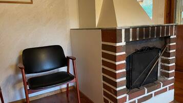 Quarto com lareira de tijolos, uma cadeira de madeira e um quadro na parede.