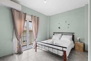 Um quarto com cama, mesa de cabeceira, janela com cortinas e ar condicionado fixado na parede.