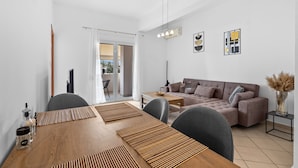 Uma sala de estar moderna com uma mesa de jantar de madeira, sofás cinzas e uma porta de vidro que dá para uma varanda.